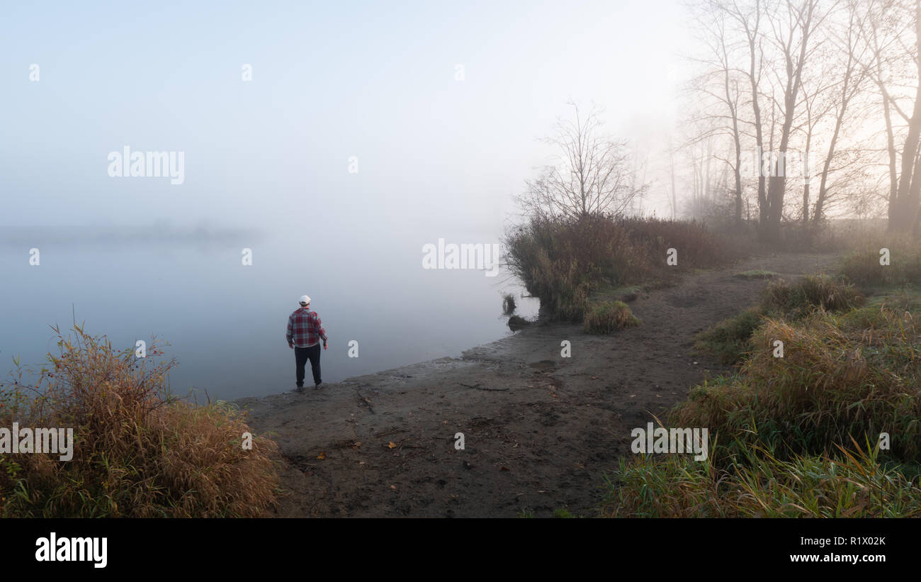 Man standing on river bank looking into the fog at sunrise Stock Photo ...