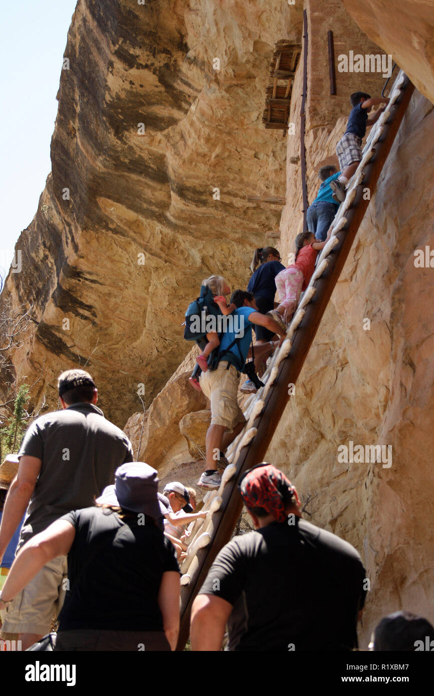 Parent and children climbing a long ladder up to cliff dwellings at ...
