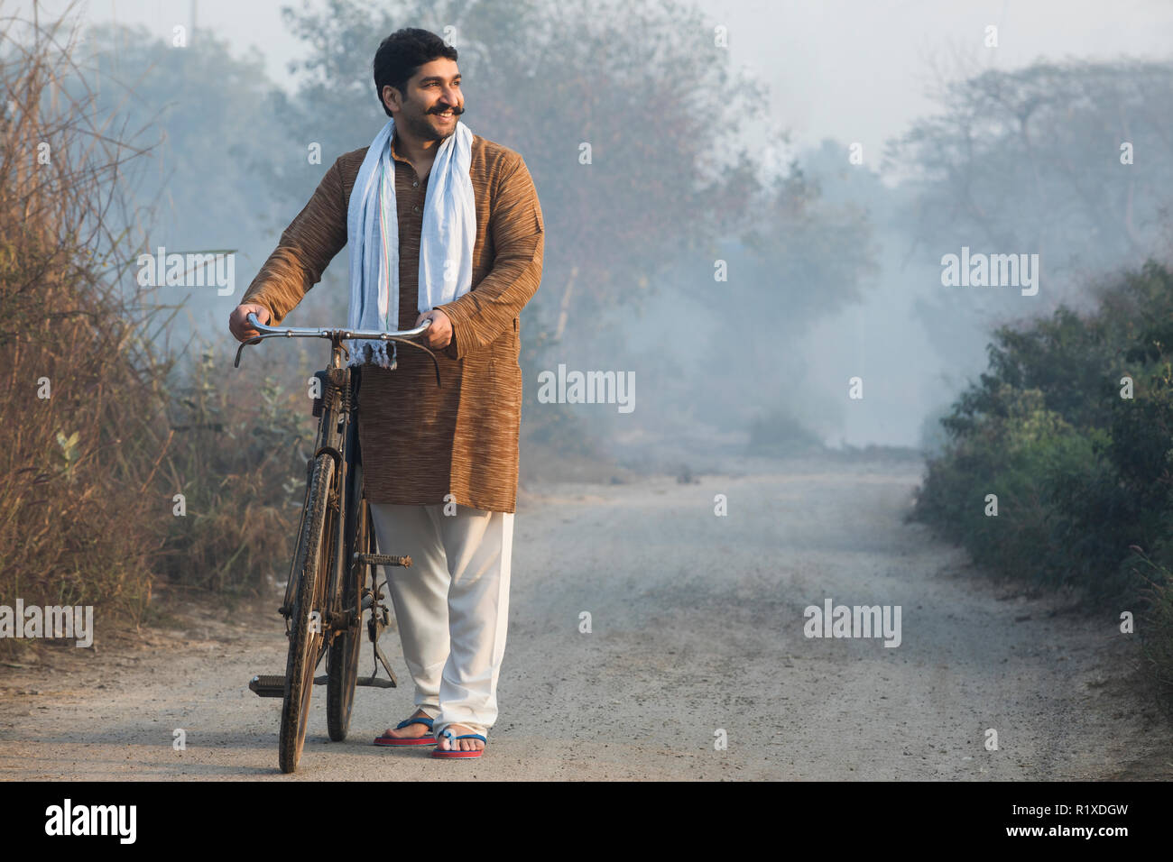 Village man standing on the street holding his bicycle looking away on ...