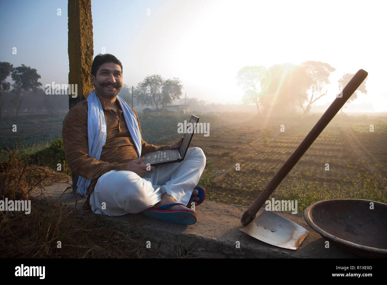 Happy looking farmer sitting near his agriculture field with a spade ...