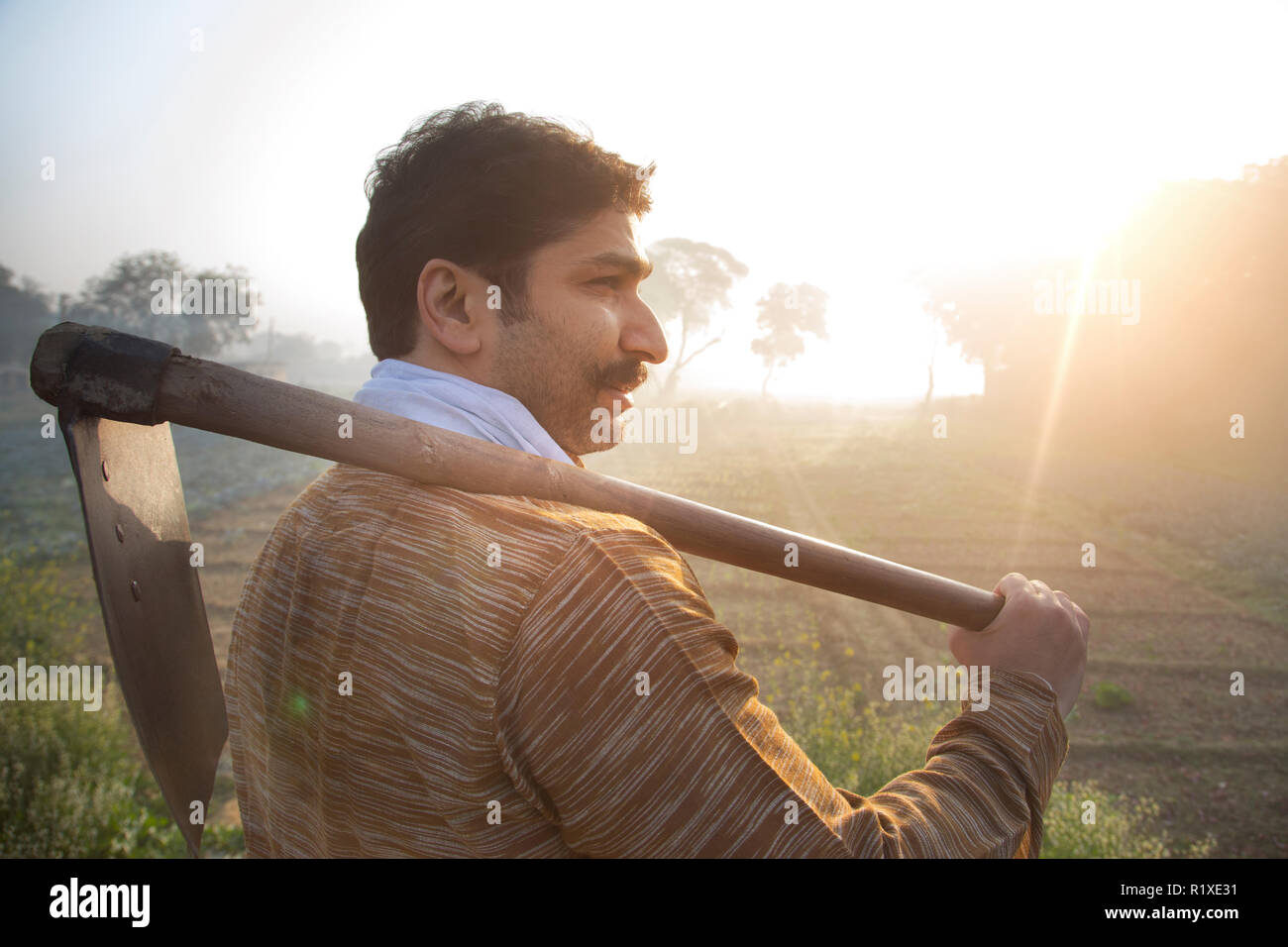 Side view of a farmer walking in his agriculture field carrying a spade ...