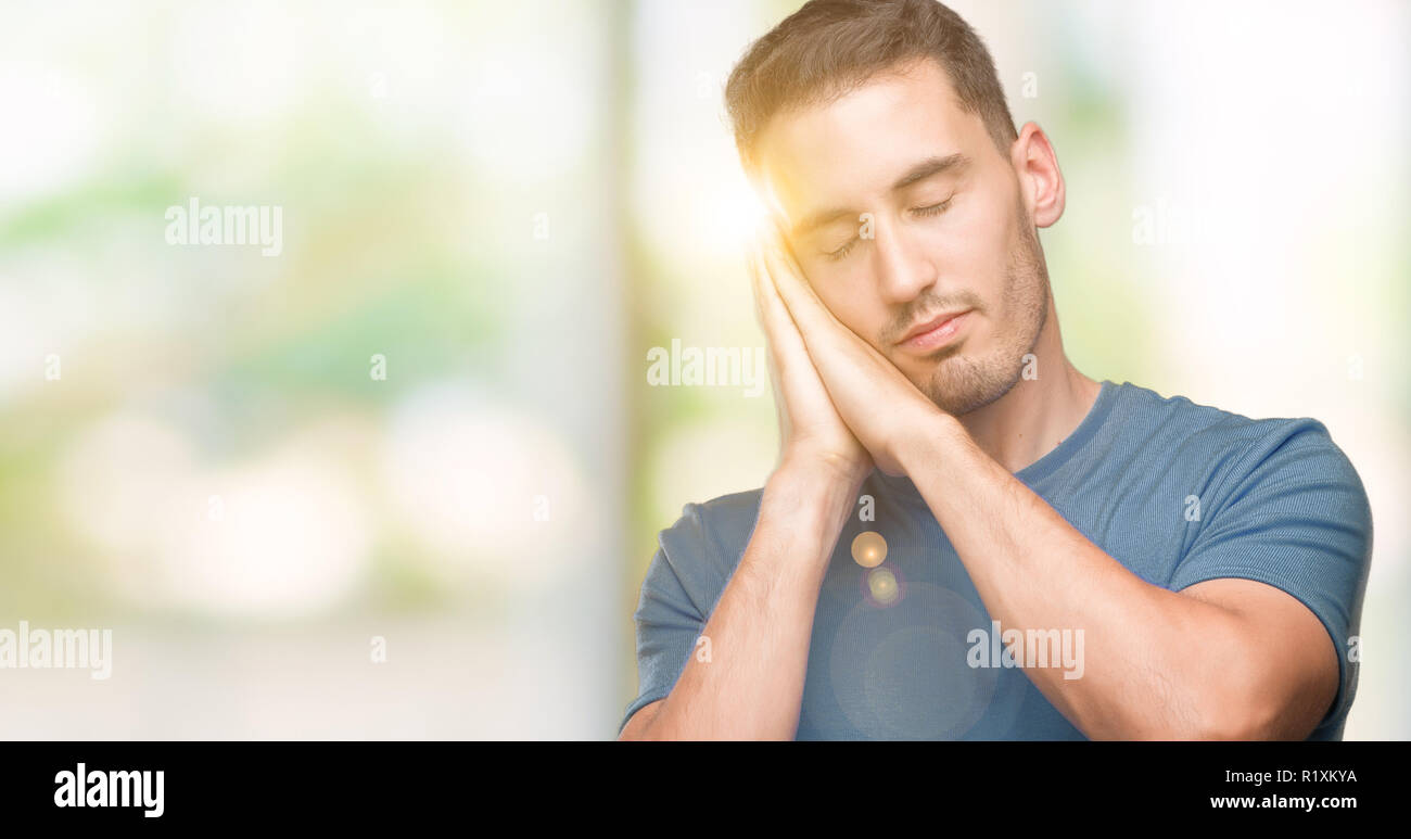 Handsome young casual man sleeping tired dreaming and posing with hands ...
