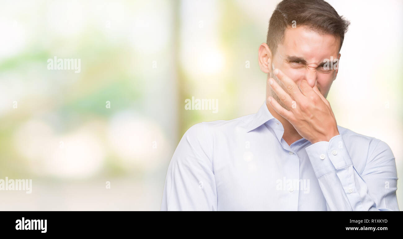 Handsome young businessman smelling something stinky and disgusting ...