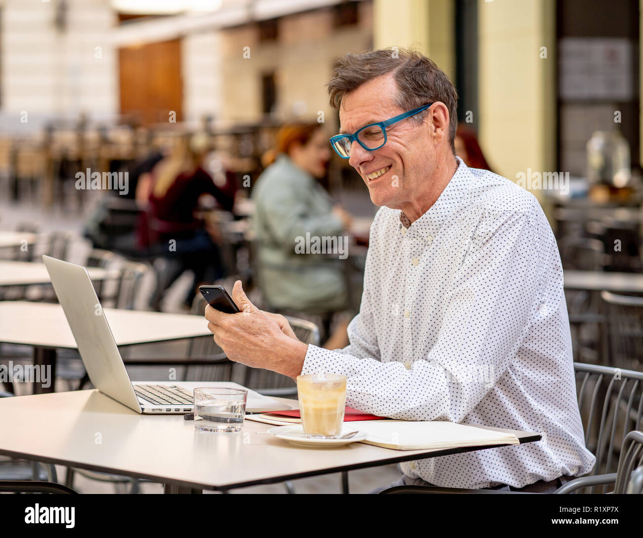 Smiling old man checking smart phone while working on computer in ...
