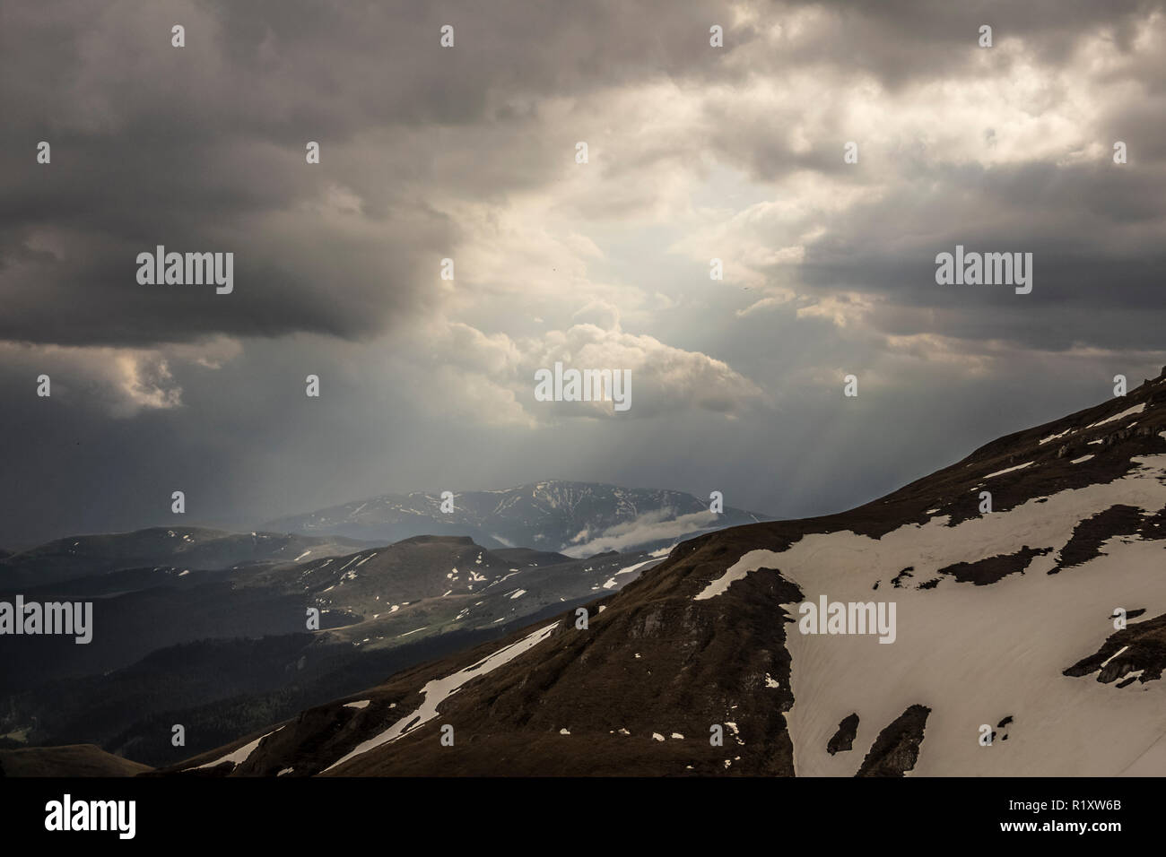 Gray rain clouds are approaching the mountain pass with sun rays ...