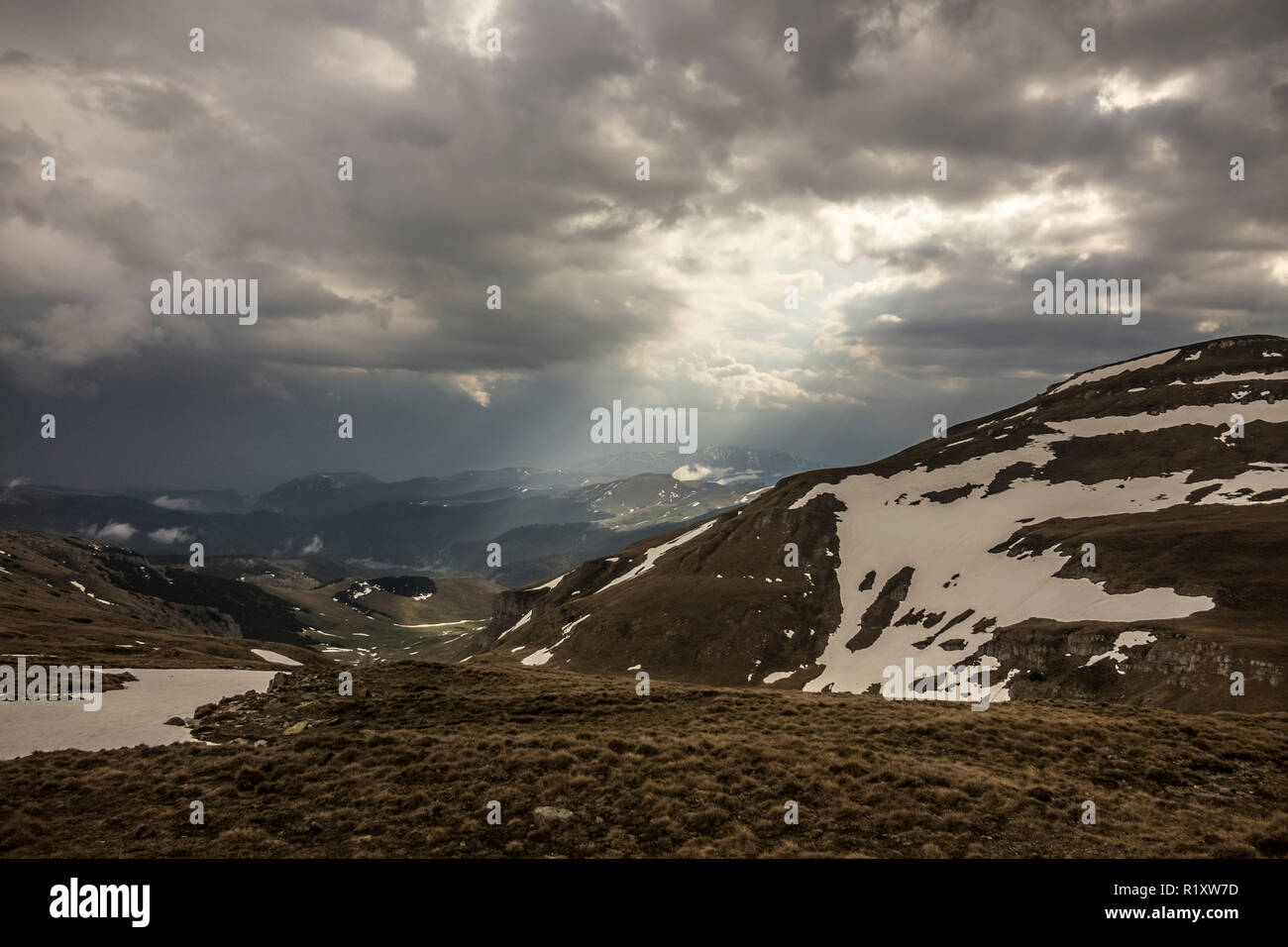 Gray rain clouds are approaching the mountain pass with sun rays ...