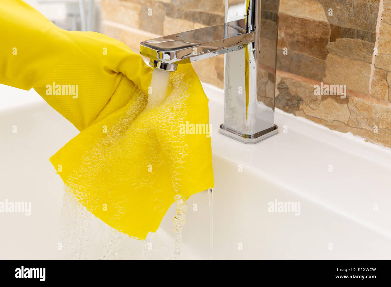 Yellow cleaning cloth being washed in sink by person wearing rubber ...