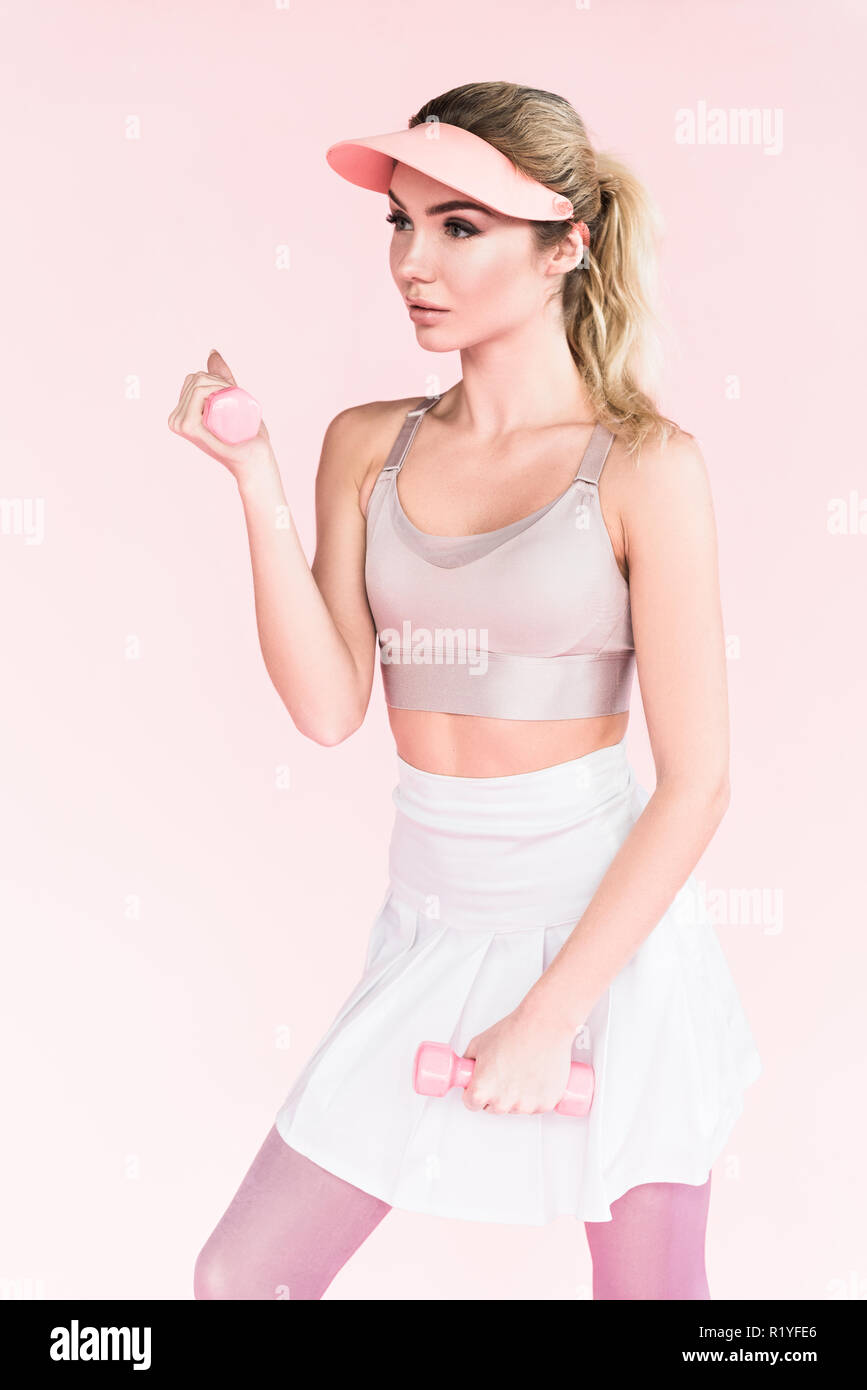 pretty female athlete in visor hat doing exercise with dumbbells on ...