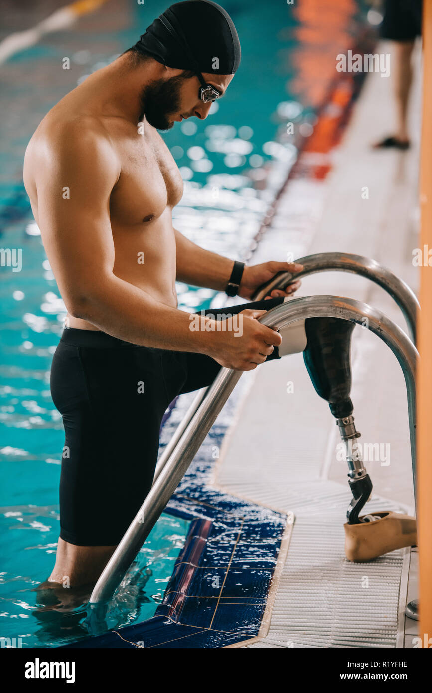 side view of handsome young swimmer with artificial leg getting out of ...