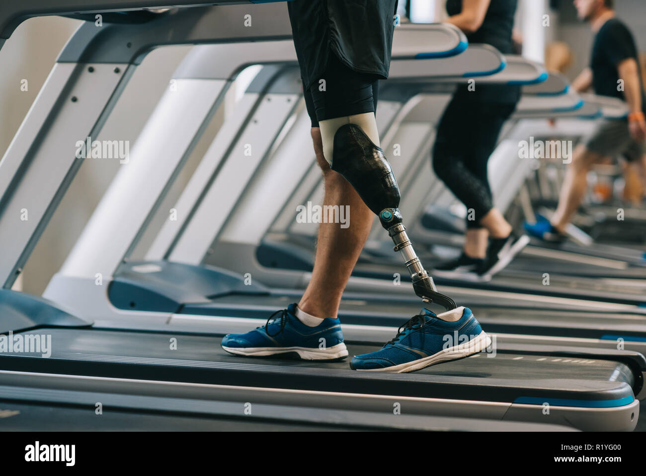 cropped shot of man with artificial leg walking on treadmills at gym ...