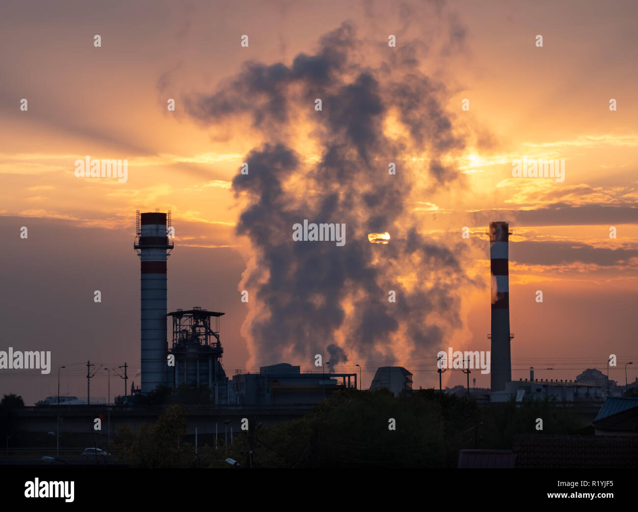 Sunrise over industrial factory with smoke rising between smokestacks ...