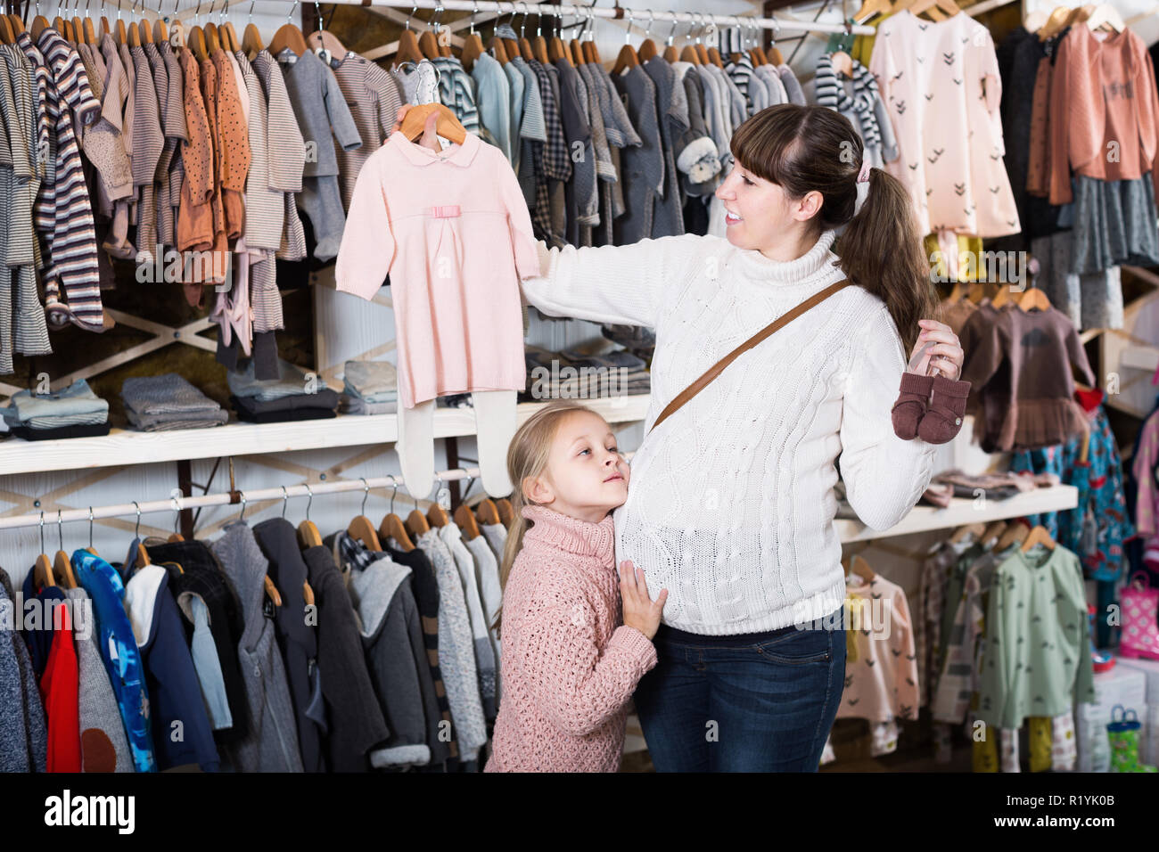Pregnant mother and daughter purchasing clothes for baby in children’s ...