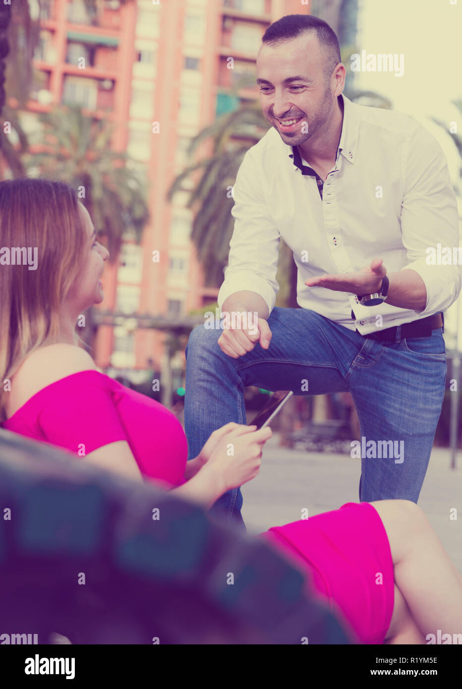 Guy is talking with smiling stranger woman who is sitting on the bench ...