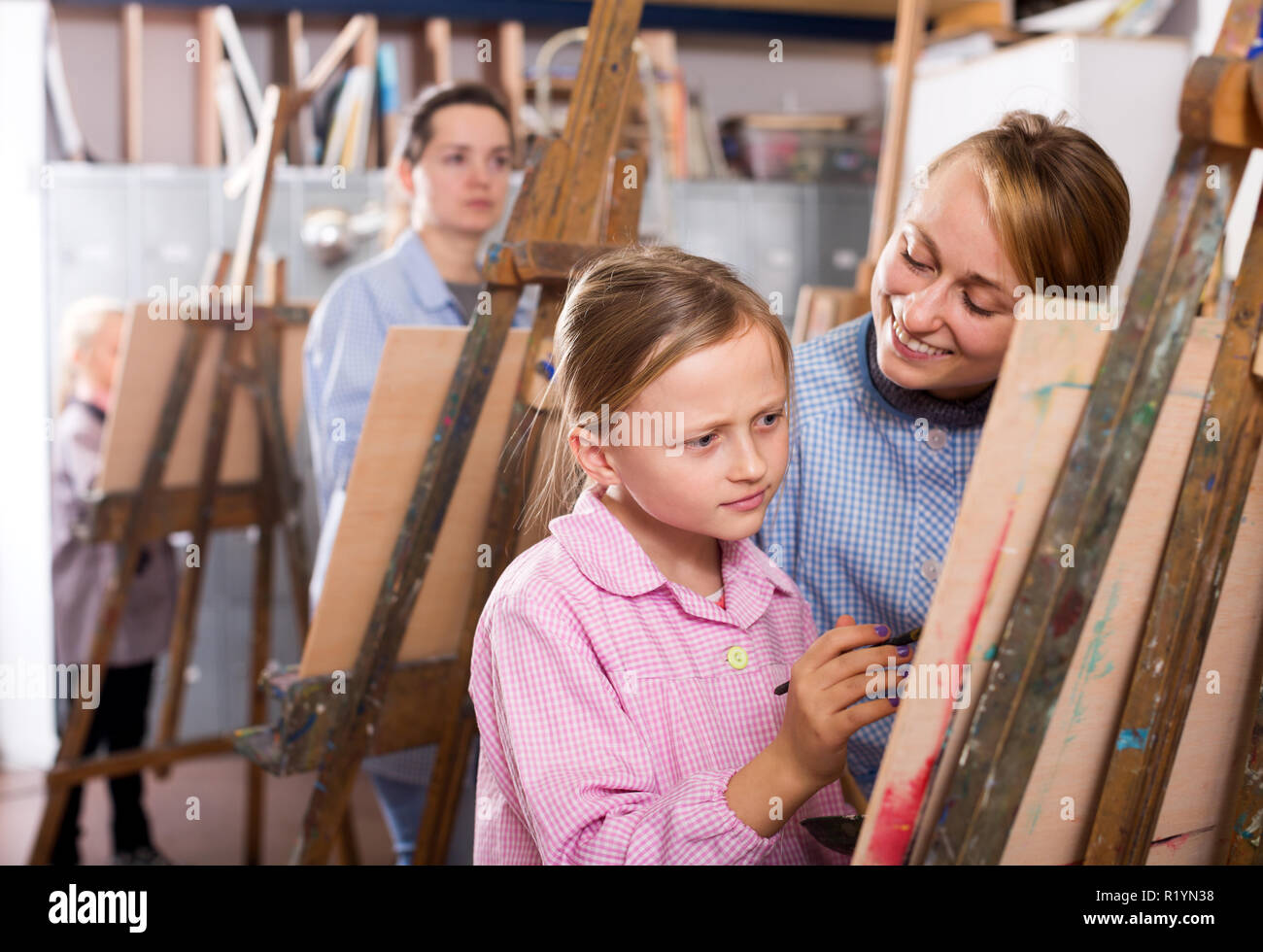 Happy female teacher helping girl during painting class at art studio ...