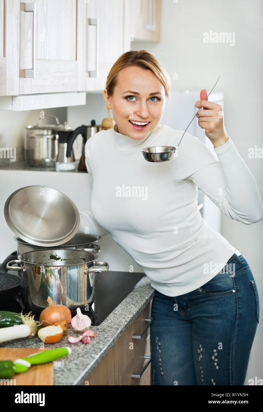 Smiling cheerful positive long-haired girl cooking soup at kitchen ...
