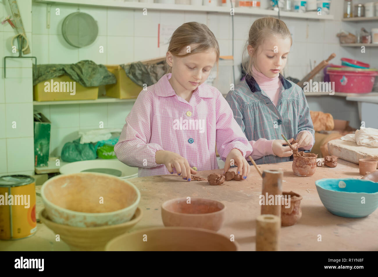Smiling schoolgirls learning to make ceramics during arts and crafts ...