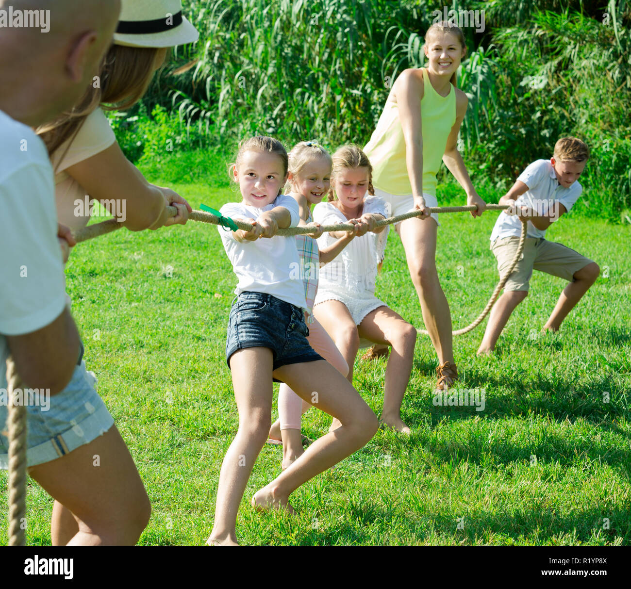 Kids with moms and dads playing tug of war during joint outdoors games ...