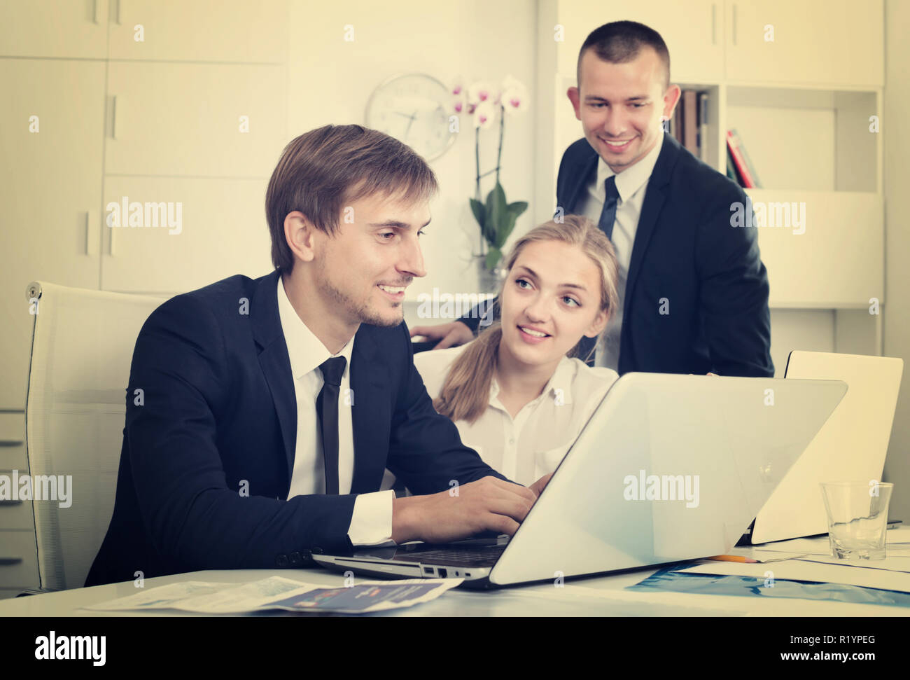 Three happy coworkers working on computers together in company office ...