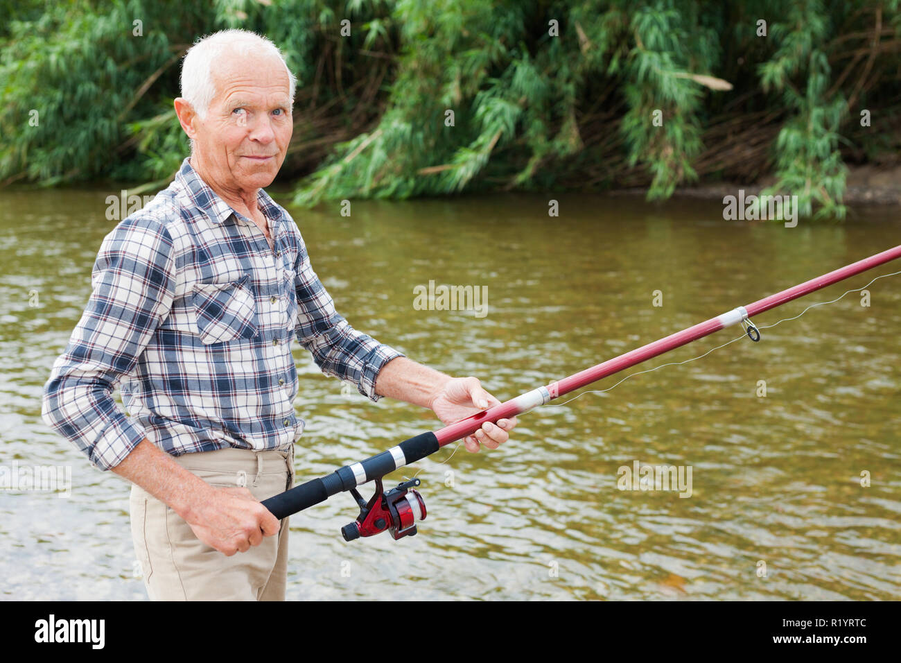 Positive adult man with rod relaxing and enjoying fishing by lakeside ...
