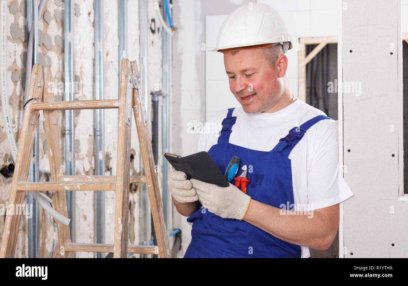 Smiling workman using phone during break in work at indoors building ...