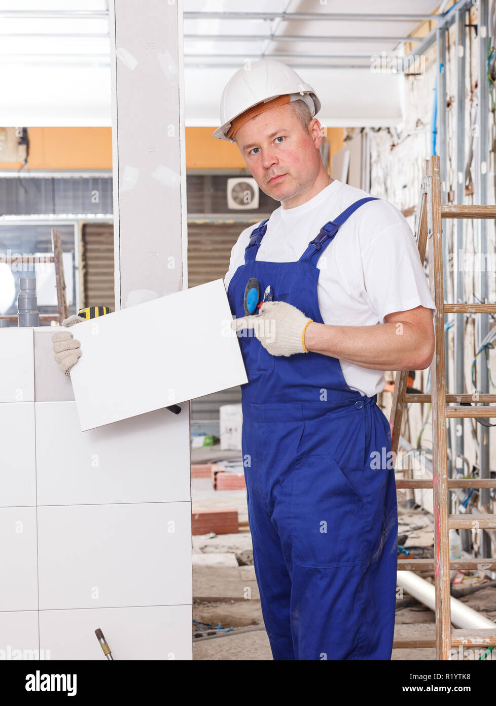 Focused construction worker engaged in wall tiling work during ...