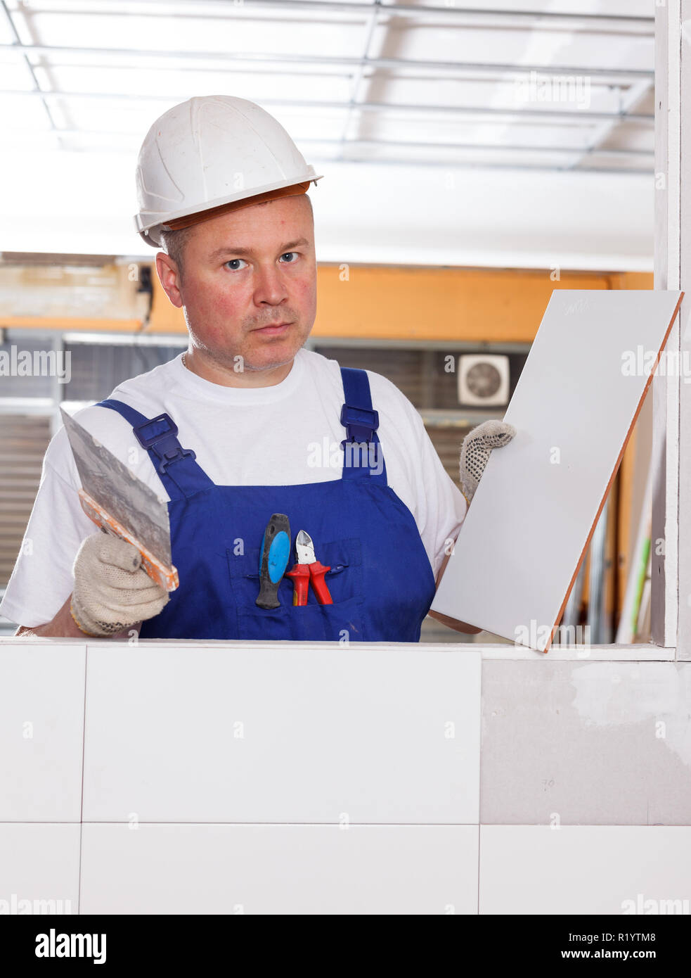 Focused construction worker engaged in wall tiling work during ...
