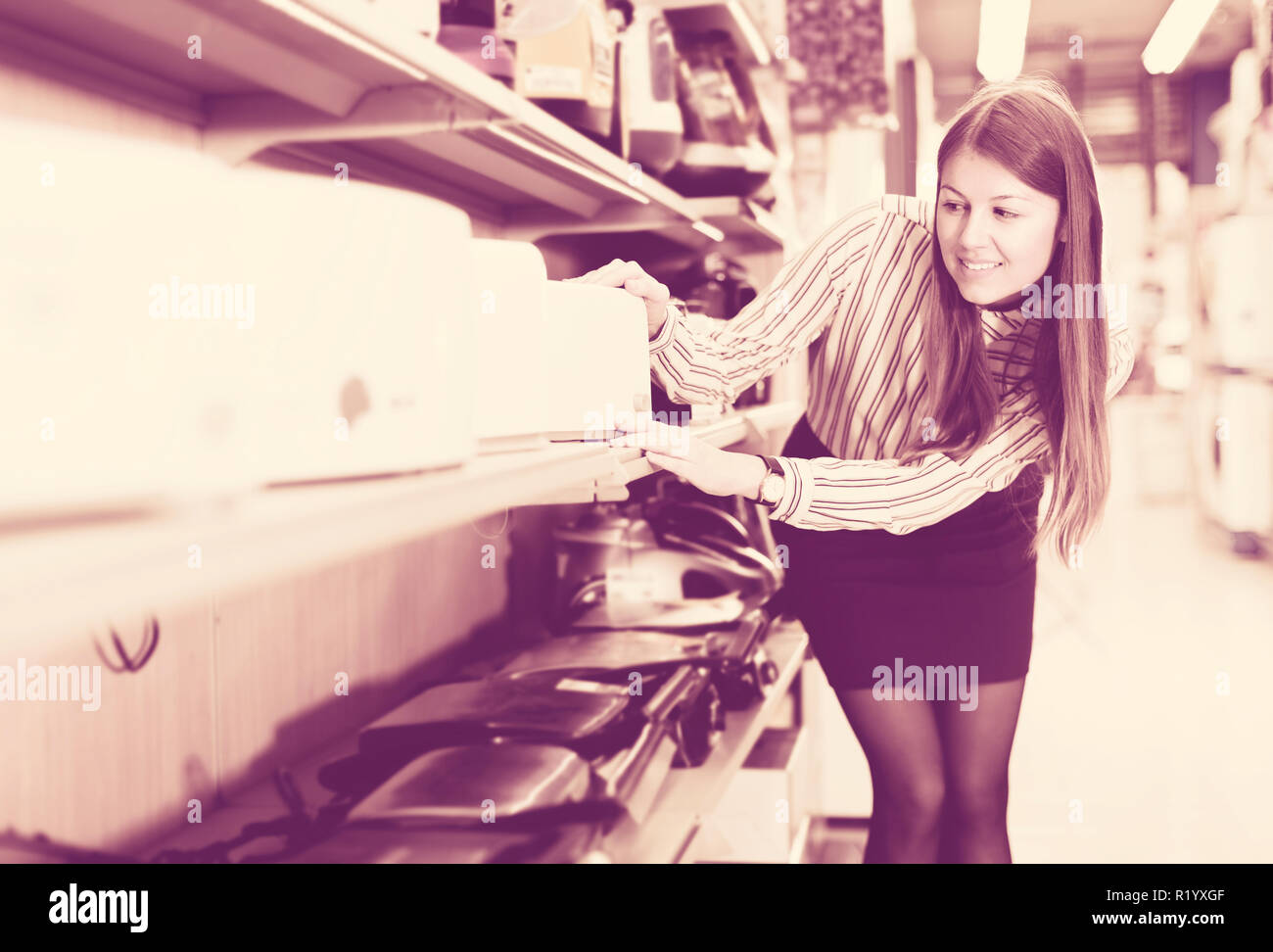 Positive girl looking for new modern toaster in kitchen appliances ...