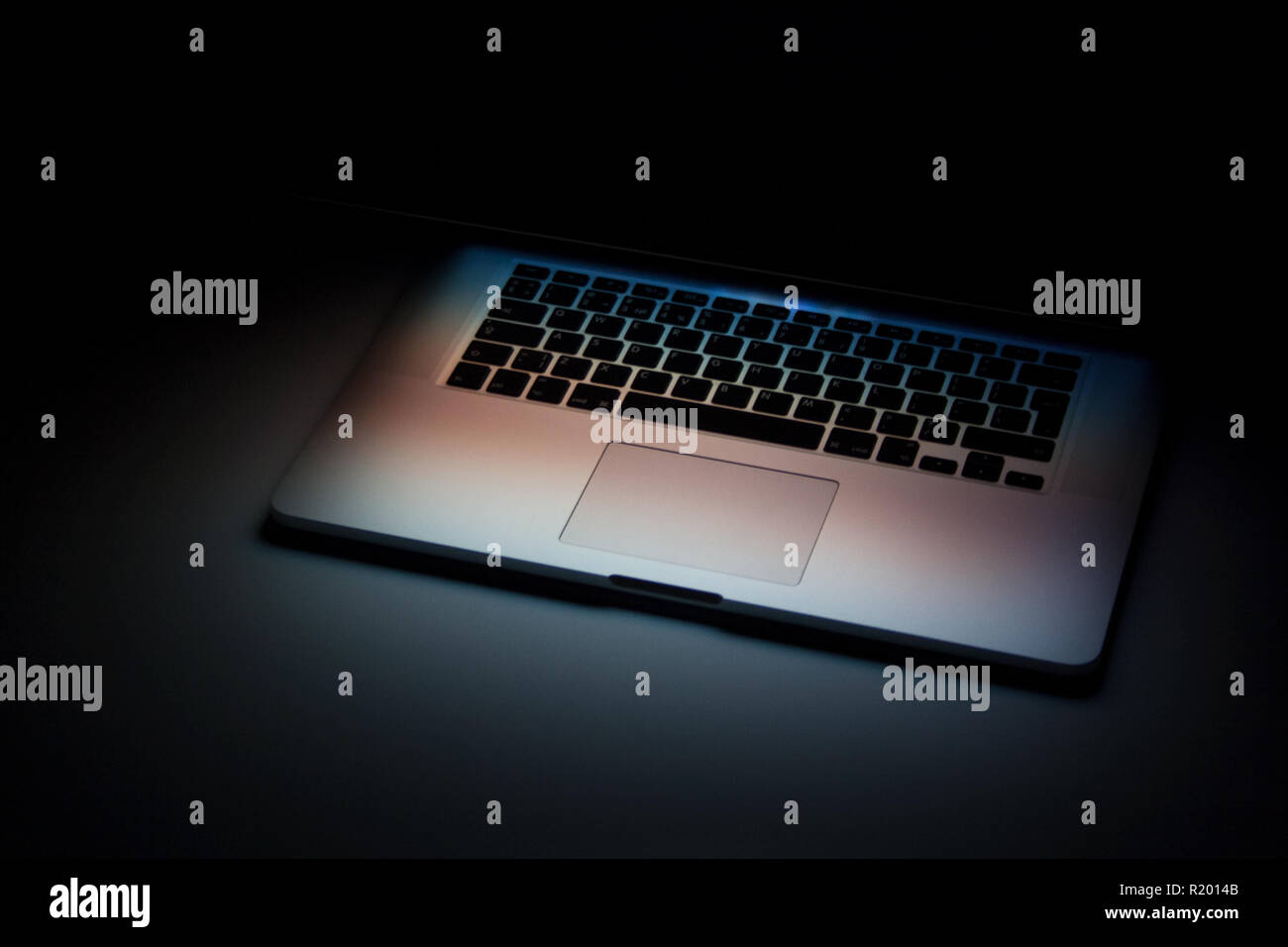 Half closed silver aluminium laptop with screen light isolated on dark ...