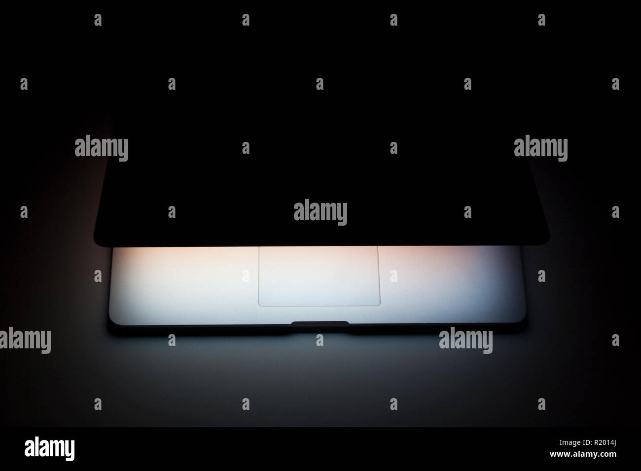 Half closed silver aluminium laptop with screen light isolated on dark ...