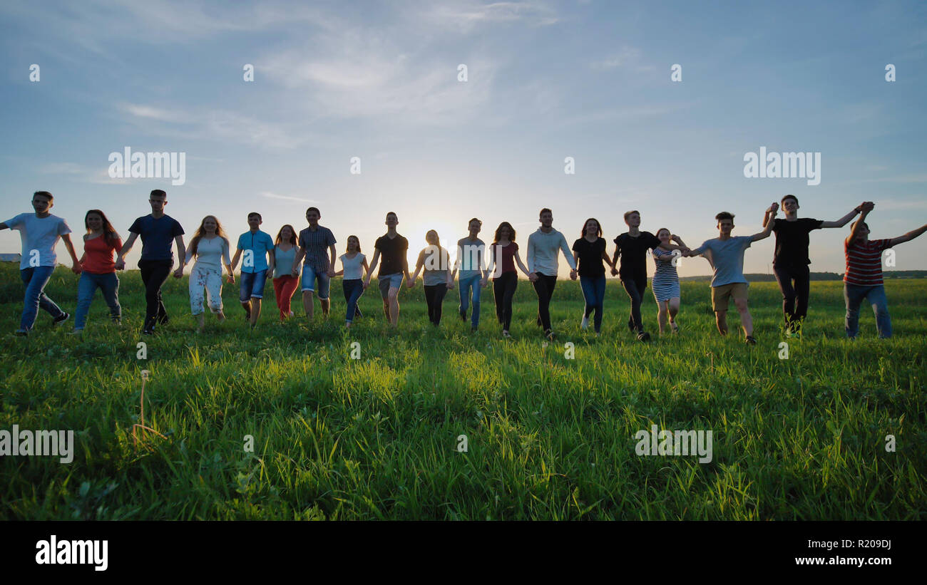 Silhouettes of nineteen friends holding hands on a sunset background ...