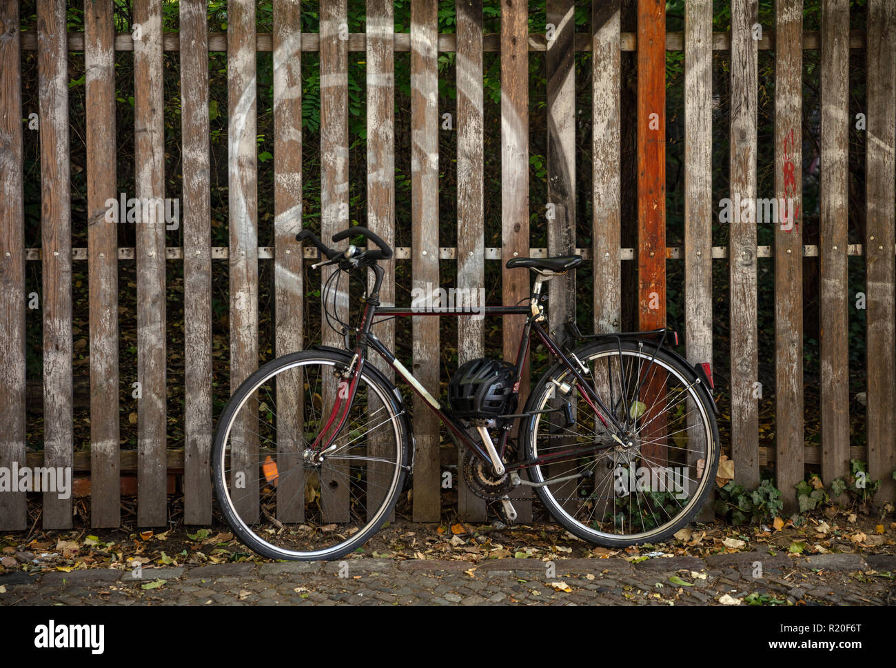 A black racing bicycle parked against a wooden fence with a black ...