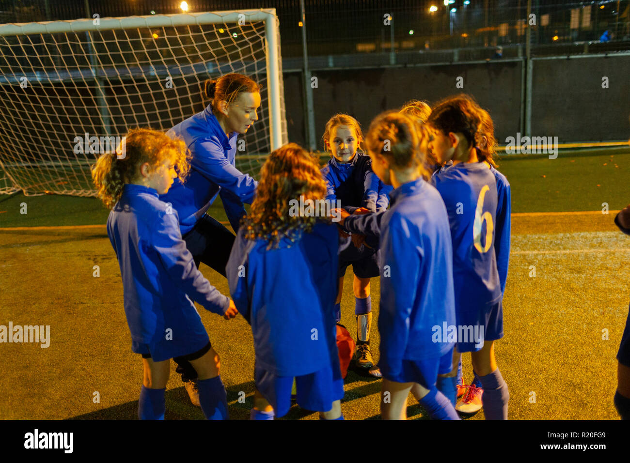 Soccer coach and girls soccer team in huddle on field at night Stock ...