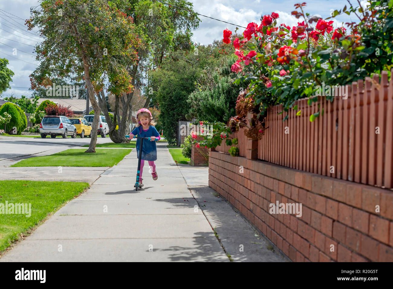 Young girl riding a kick-scooter on the street, wearing ping outfit and ...