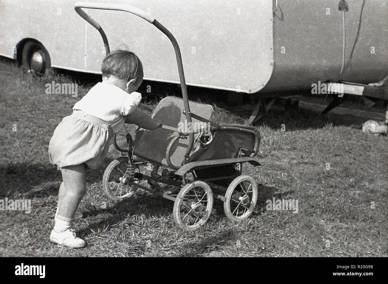 1950s, historical, infant child having fun pushing a folding metal ...