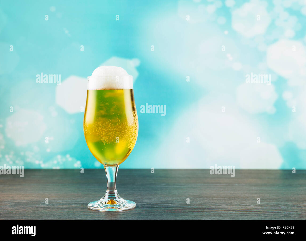 Goblet style beer glass on dark natural wooden table with light blue ...