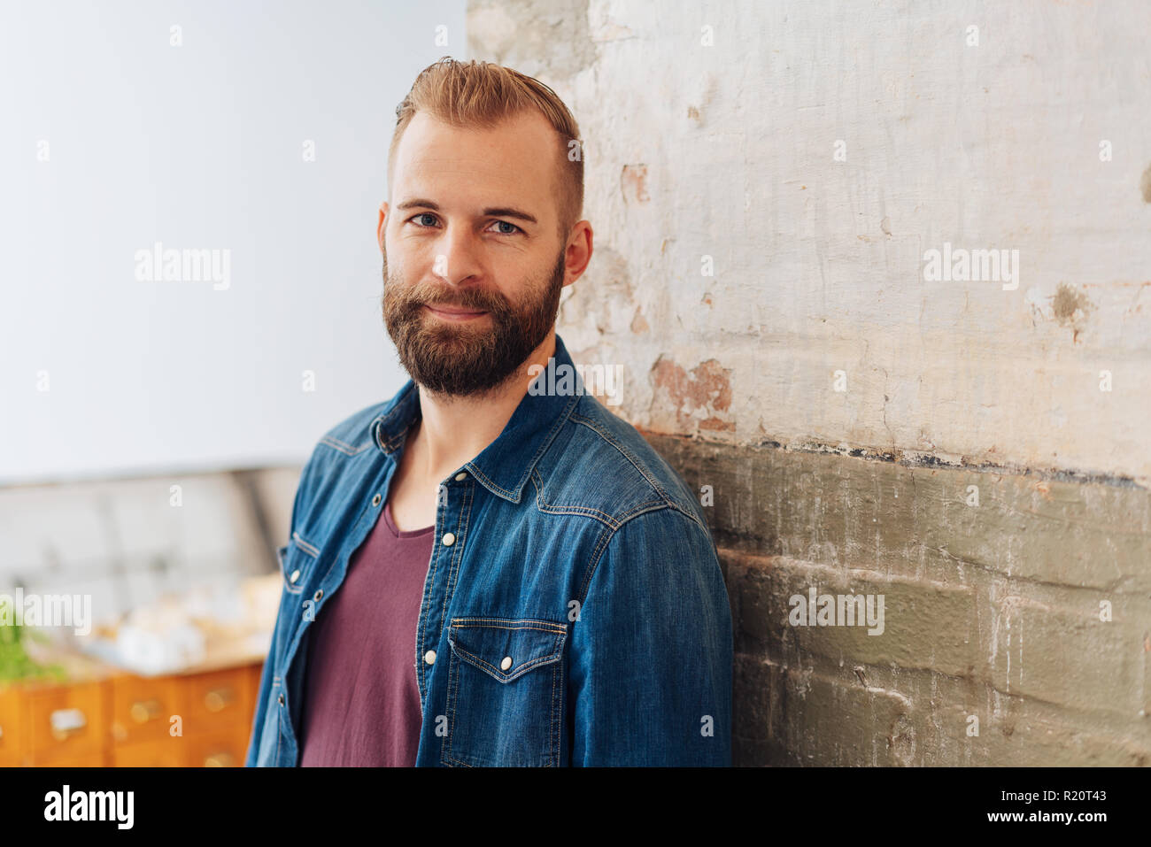 Friendly bearded man with a quiet smile leaning against an exterior ...