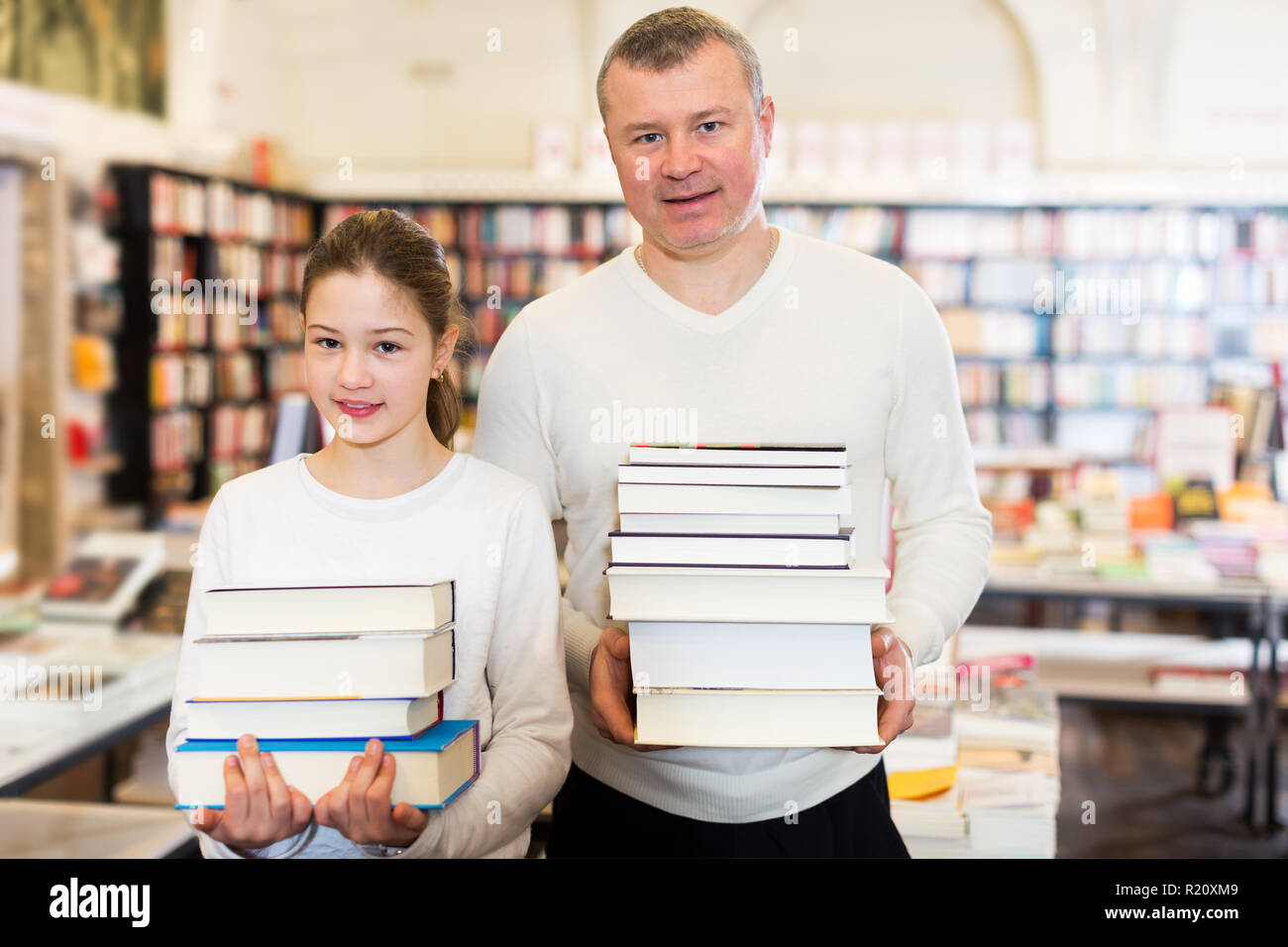 Happy little girl with her loving father holding pile of books bought ...