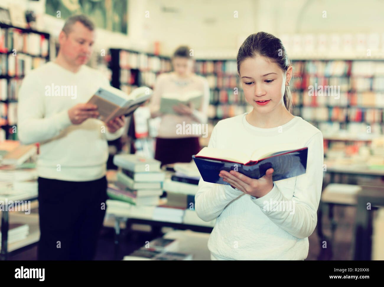 Intelligent little girl visiting a bookstore with parents searching an ...