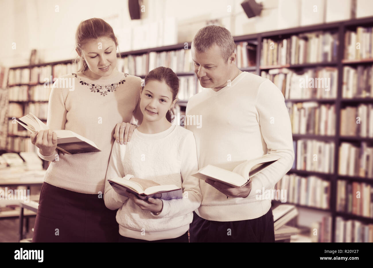 parents and happy little girl choosing books together in bookstore ...