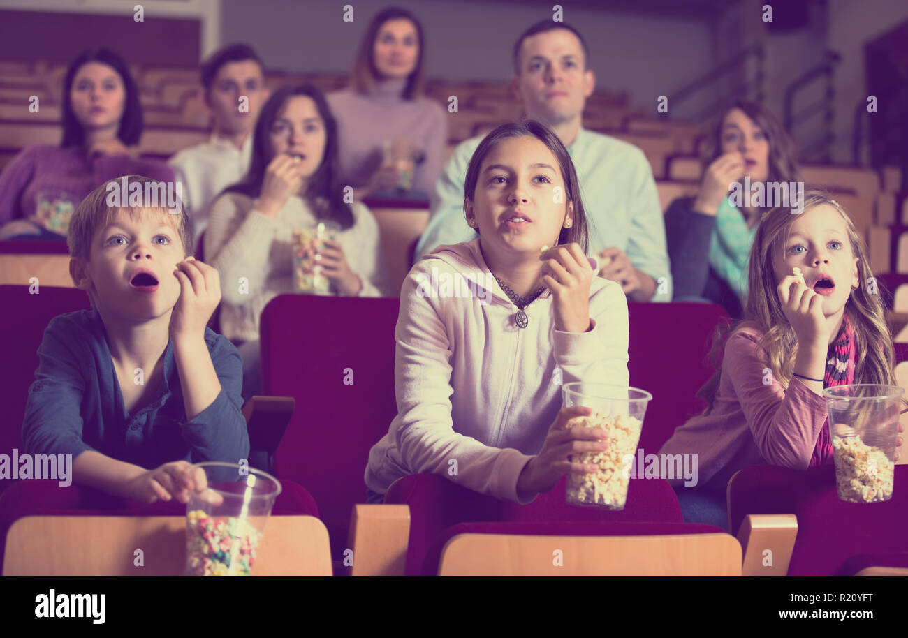 Numerous spectators eating popcorn and watching a movie at the cinema ...