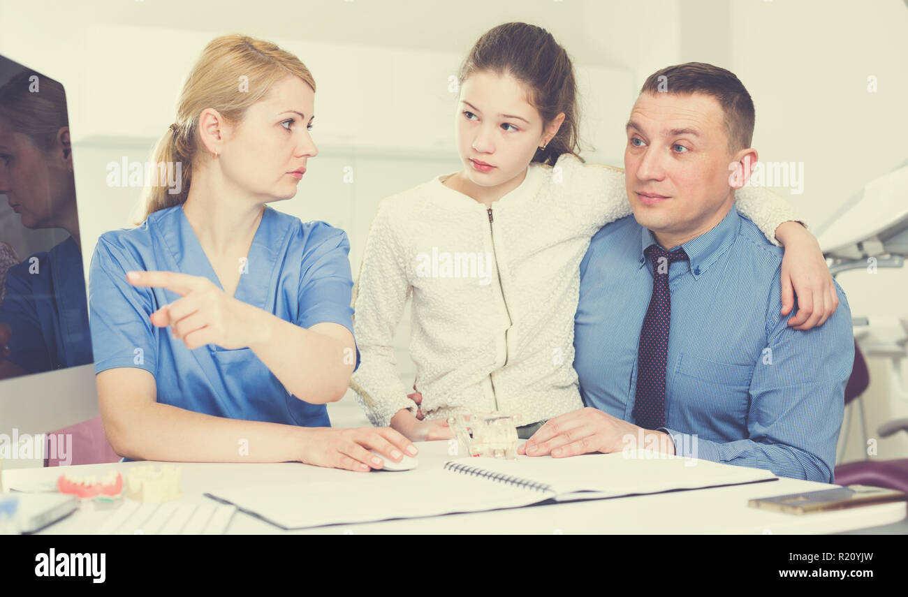 Female dentist pointing at monitor explaining diagnosis of girl patient ...