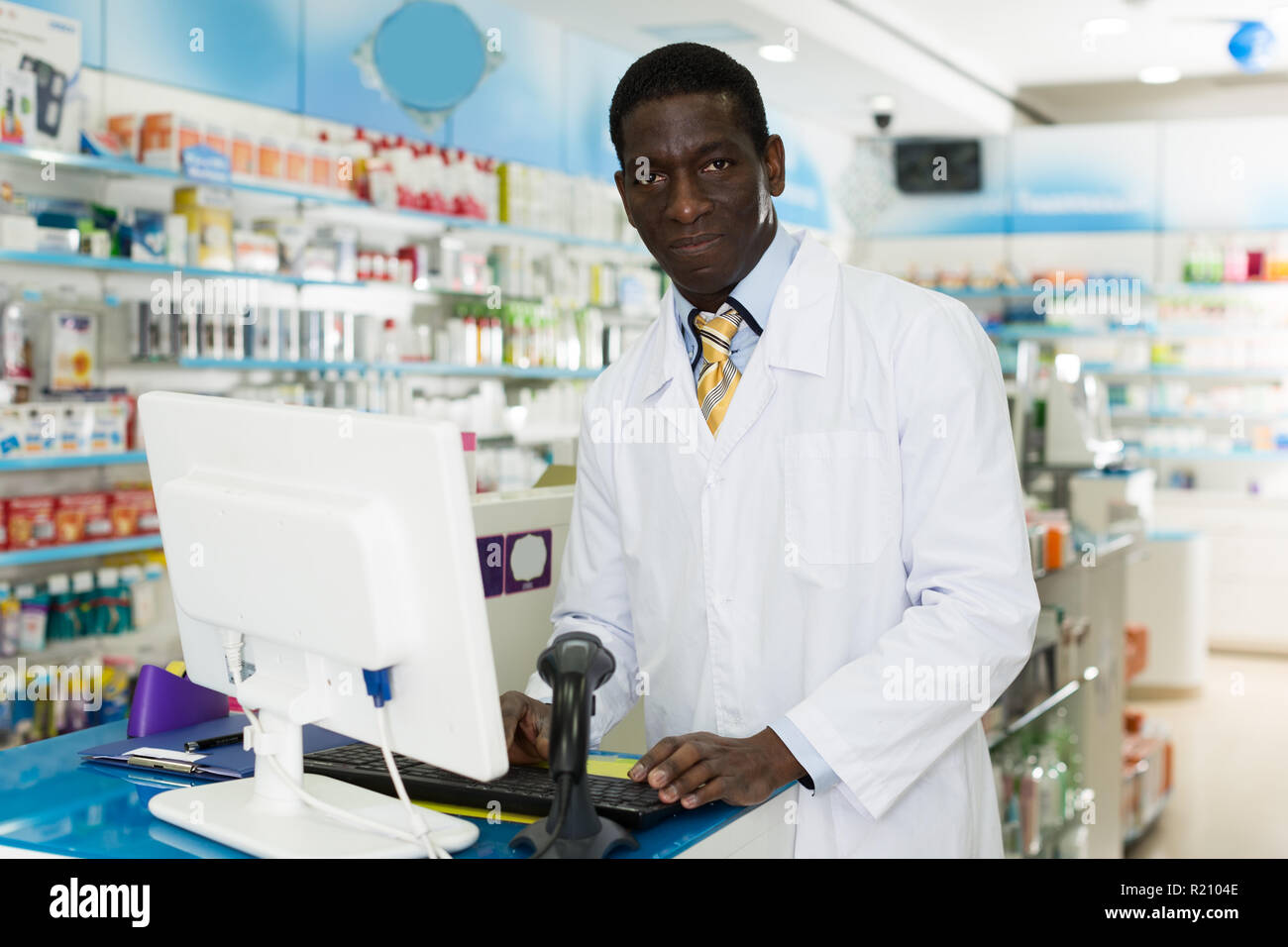 Portrait of male pharmacist standing by the computer behind counter in ...