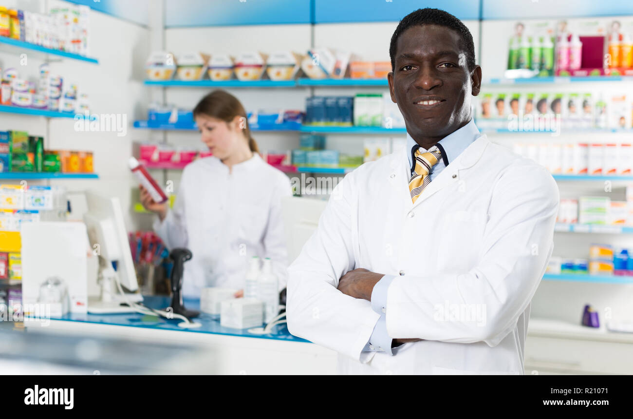 positive male pharmacist standing in interior of pharmacy Stock Photo ...