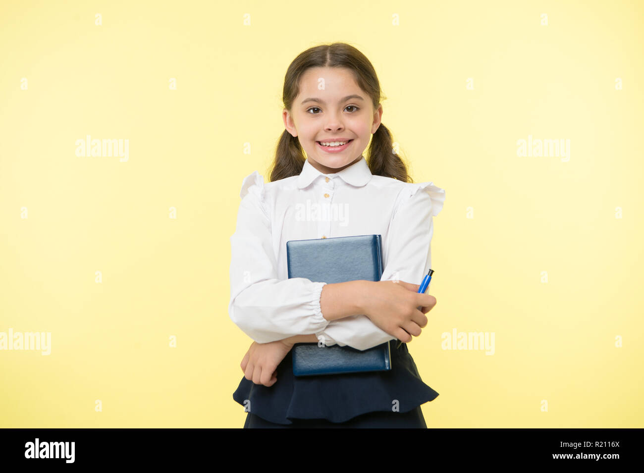 Happy schoolgirl hold book on yellow background. Little girl smile with ...
