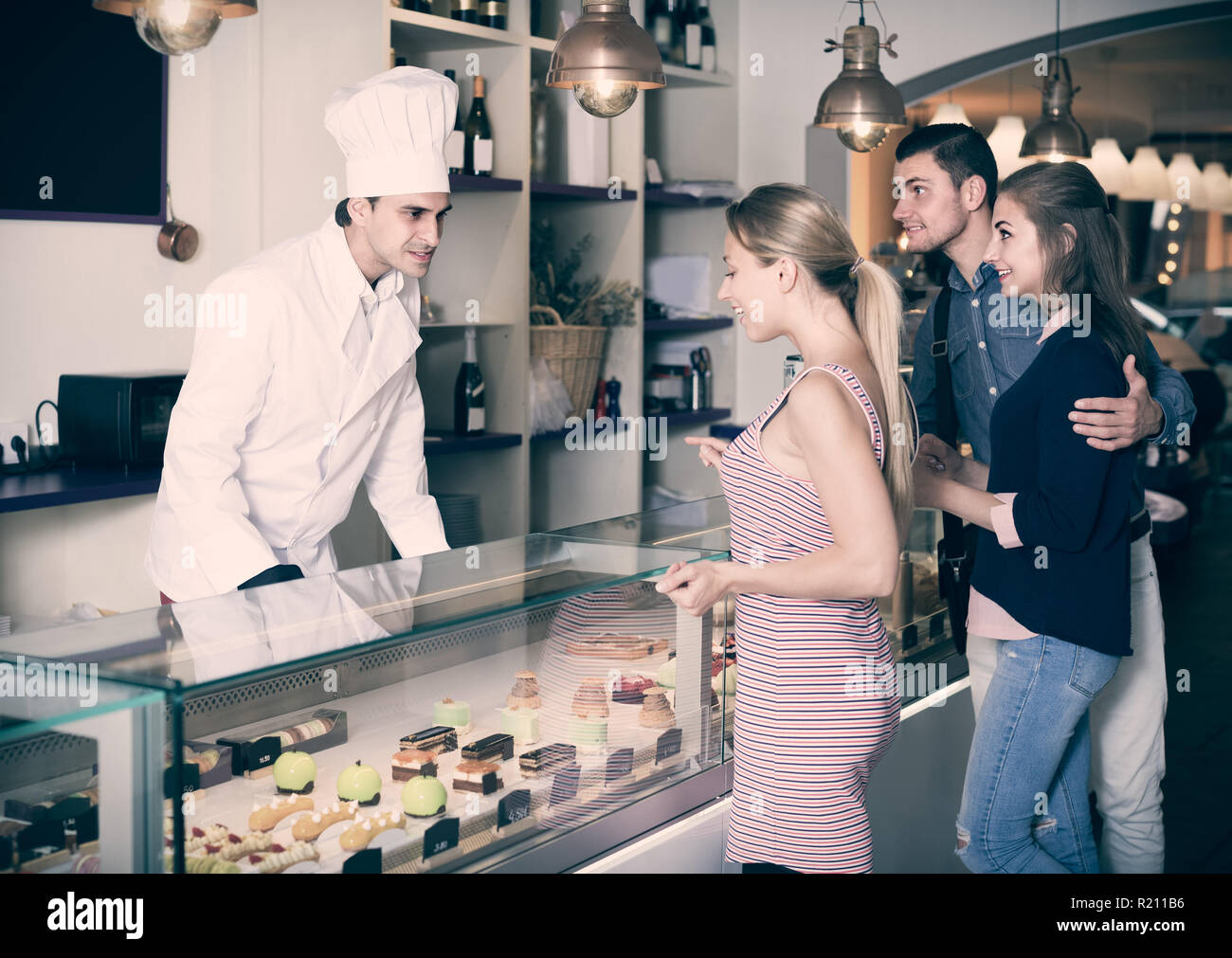 Professional chef is offering delicious cakes from showcase in pastry ...