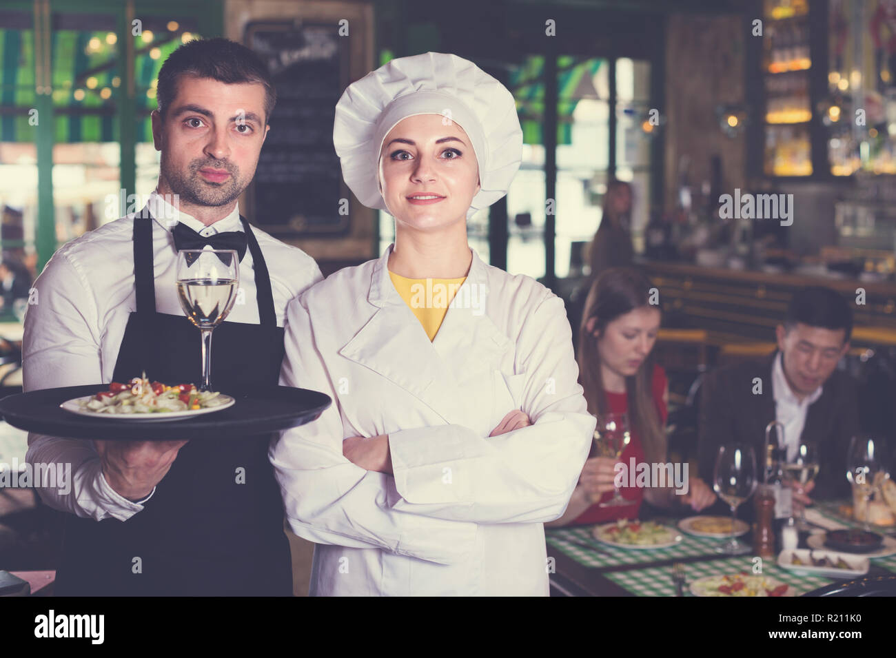Portrait of male waiter and female cook who are welcoming clients in ...