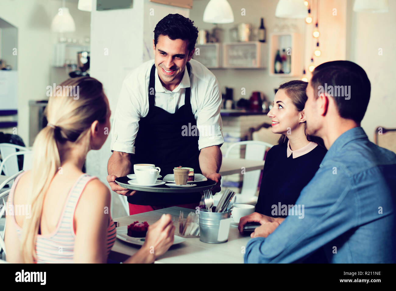 Waiter is bringing drinking and delicious desserts to clients of cafe ...