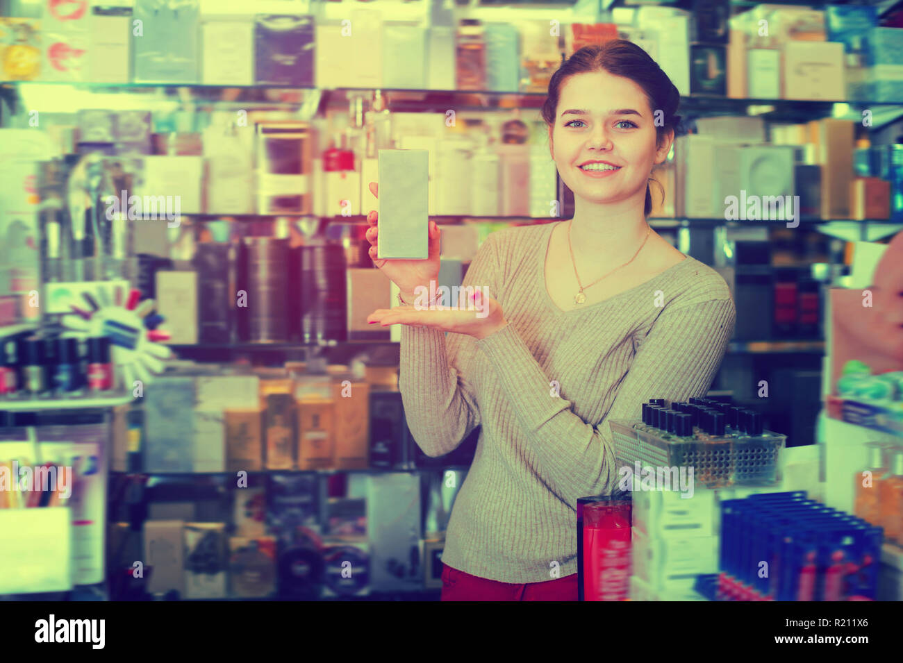 Adult female shop assistant displaying variety of perfume in cosmetics ...