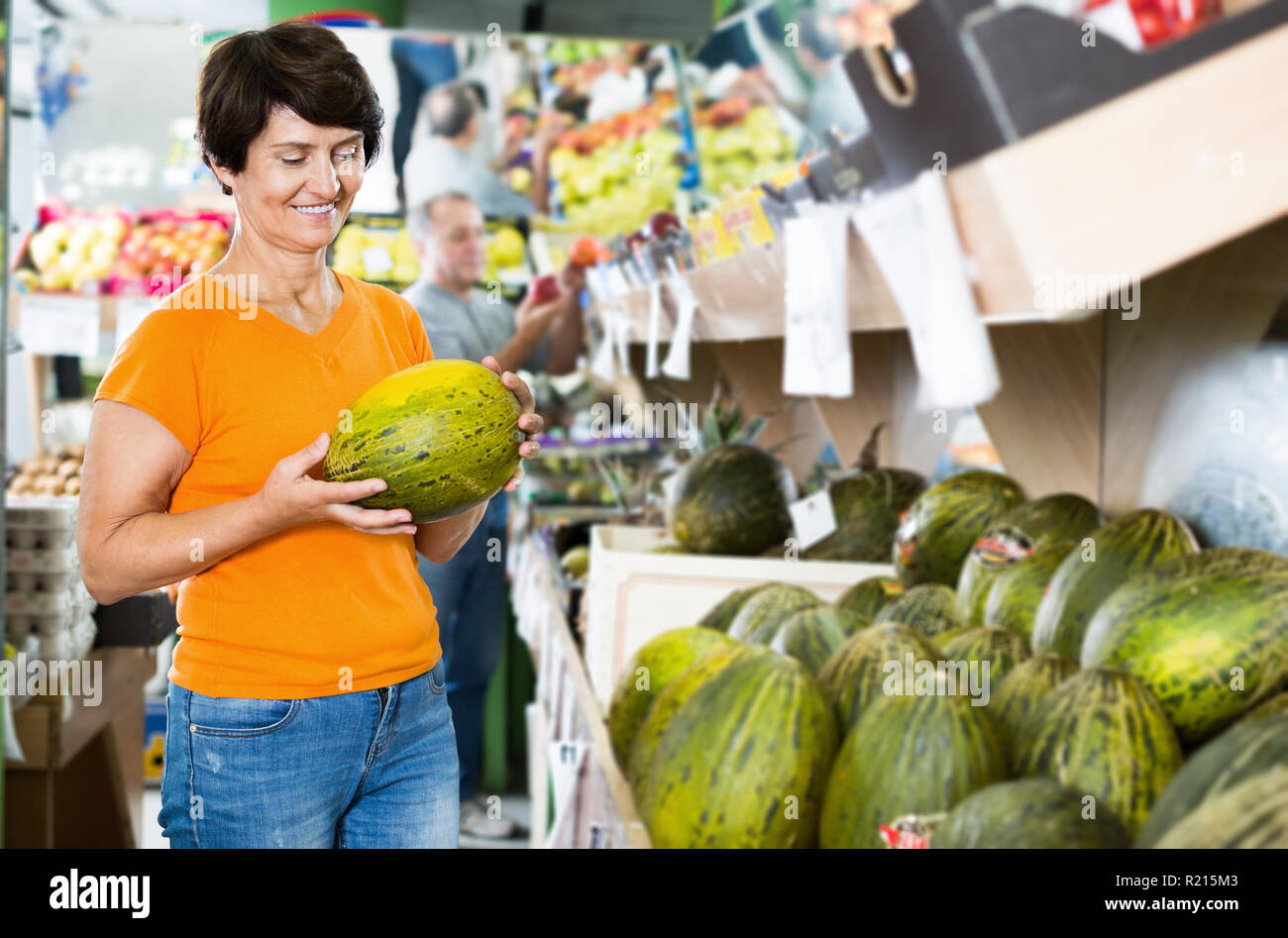Smiling mature woman is choosing green melon in the supermarket Stock ...