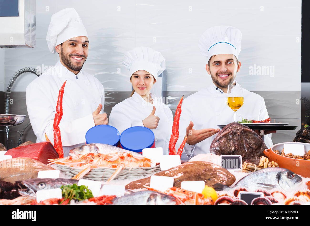 Team of fish restaurant chefs standing behind icy showcase, offering ...